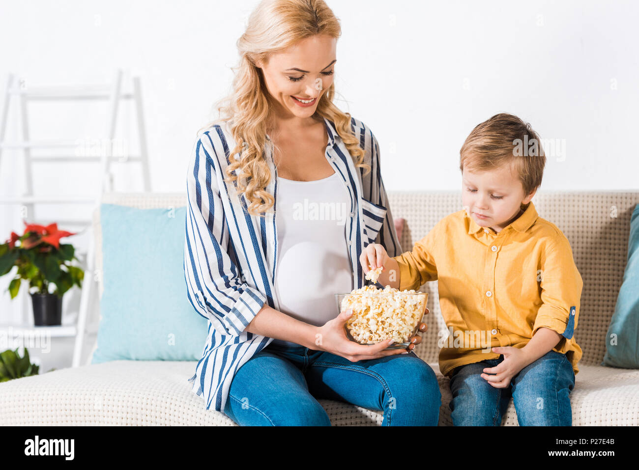 pregnant woman and cute little son eating popcorn from glass bowl at ...