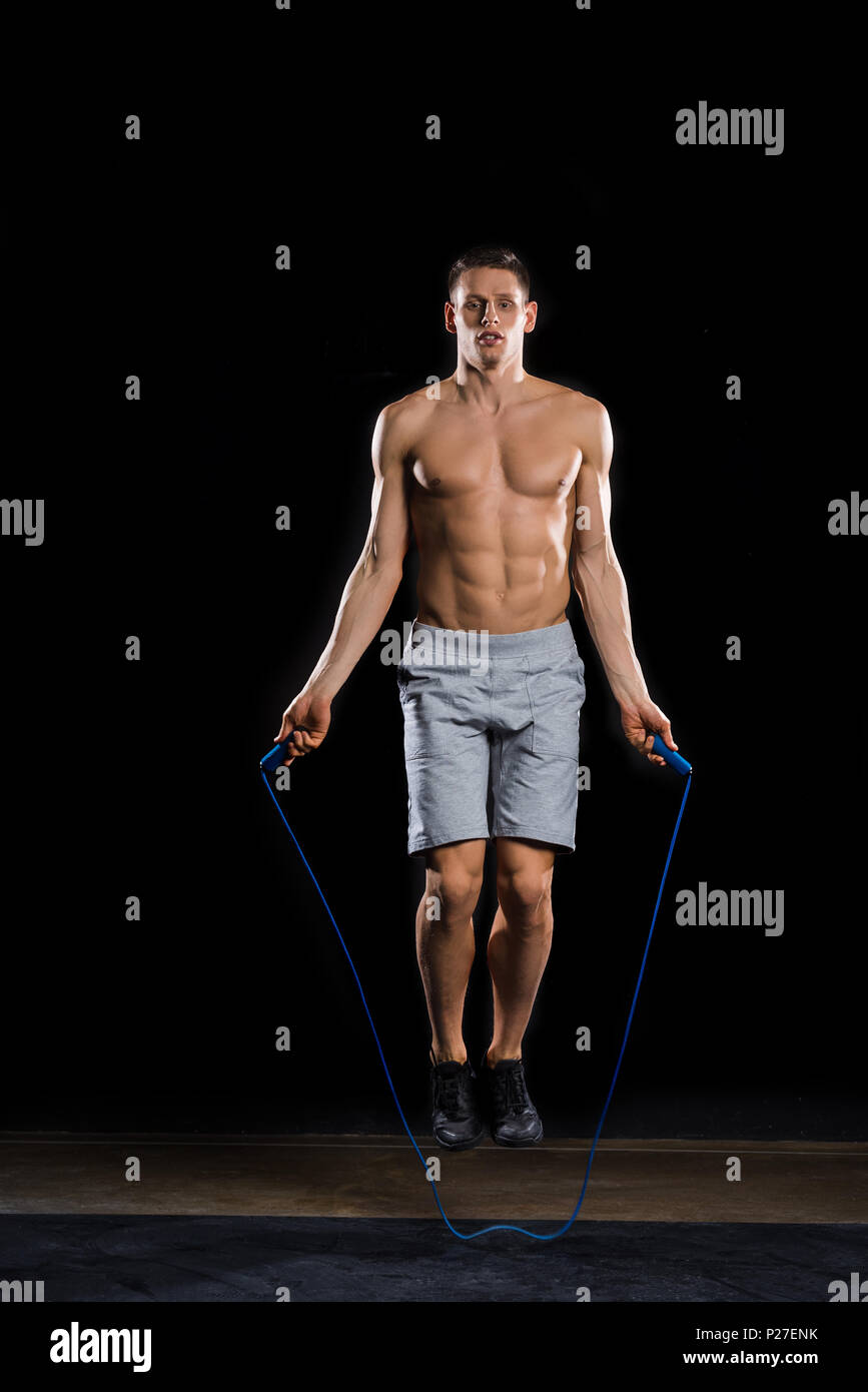 muscular shirtless sportsman jumping with skipping rope on black Stock ...