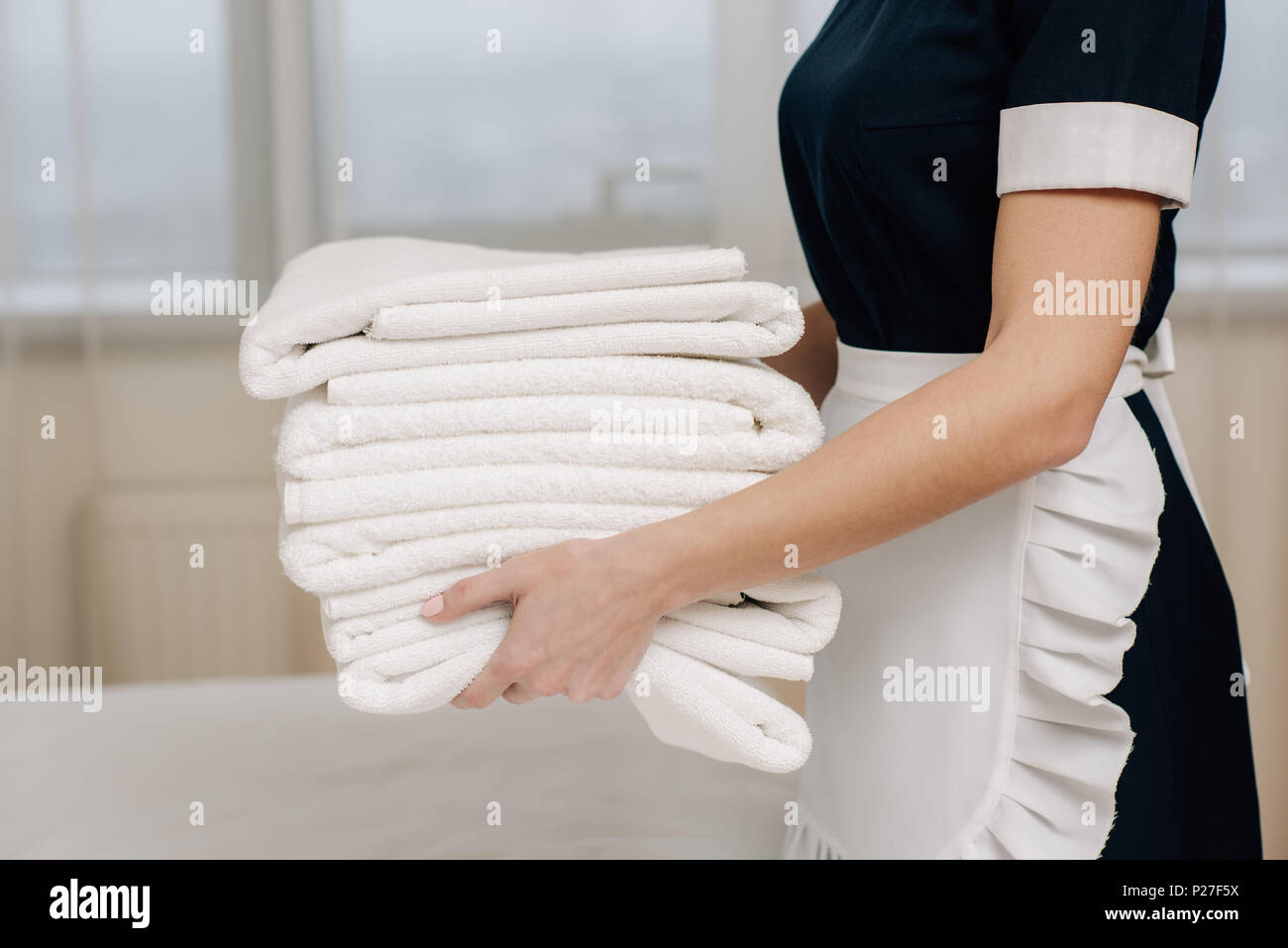 cropped shot of maid in uniform holding stack of clean towels in hotel ...