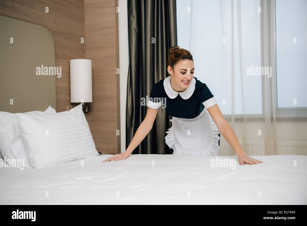 young smiling maid in uniform making bed at hotel suite Stock Photo - Alamy