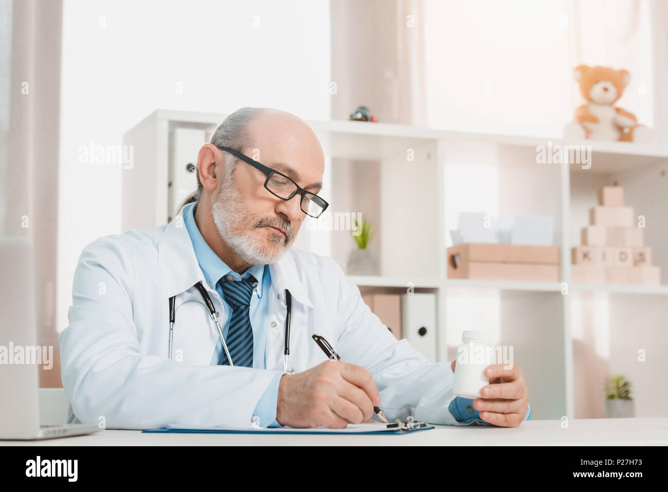 portrait of focused senior doctor making notes on notepad at workplace ...