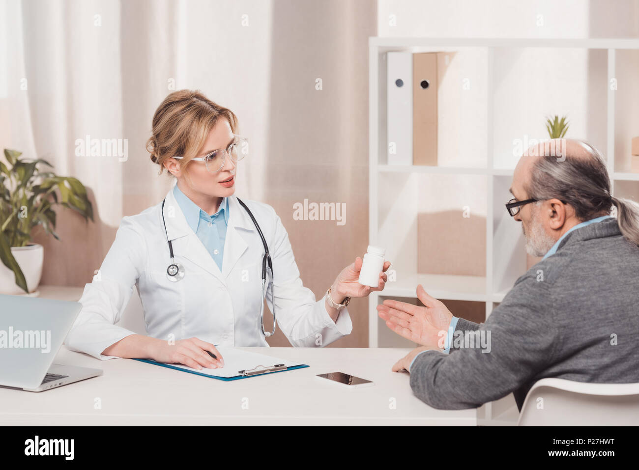 doctor in white coat and eyeglasses showing medicines to senior patient ...