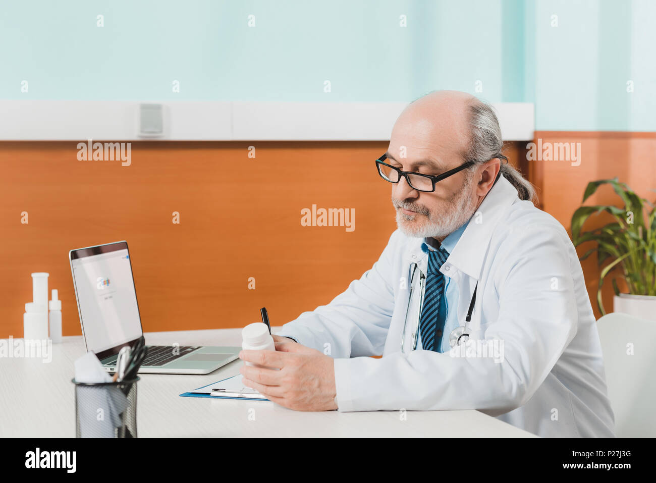 side view of focused senior doctor making notes on notepad at workplace ...