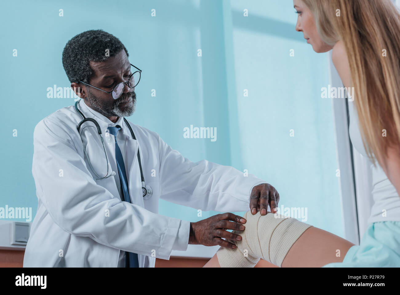 african american doctor putting on elastic bandage on patient injured ...