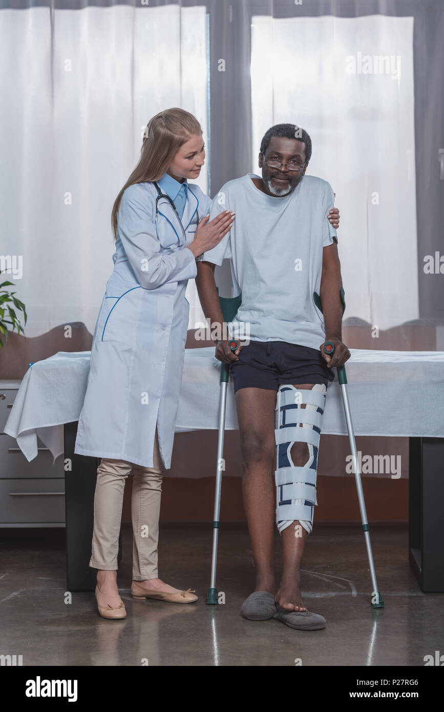 Young doctor helping stand up to african american patient with leg ...