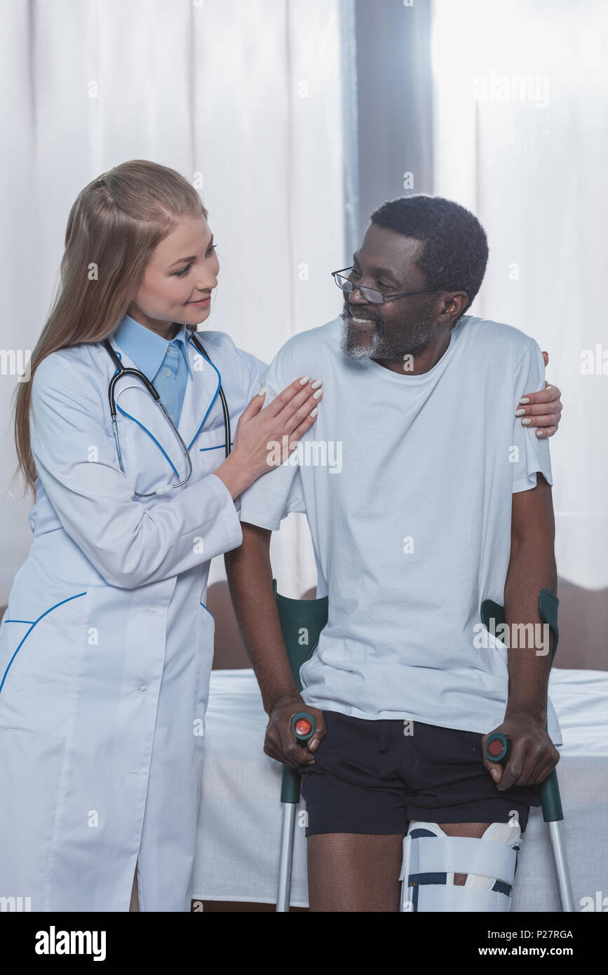 Young female doctor helping stand up to male african american patient ...