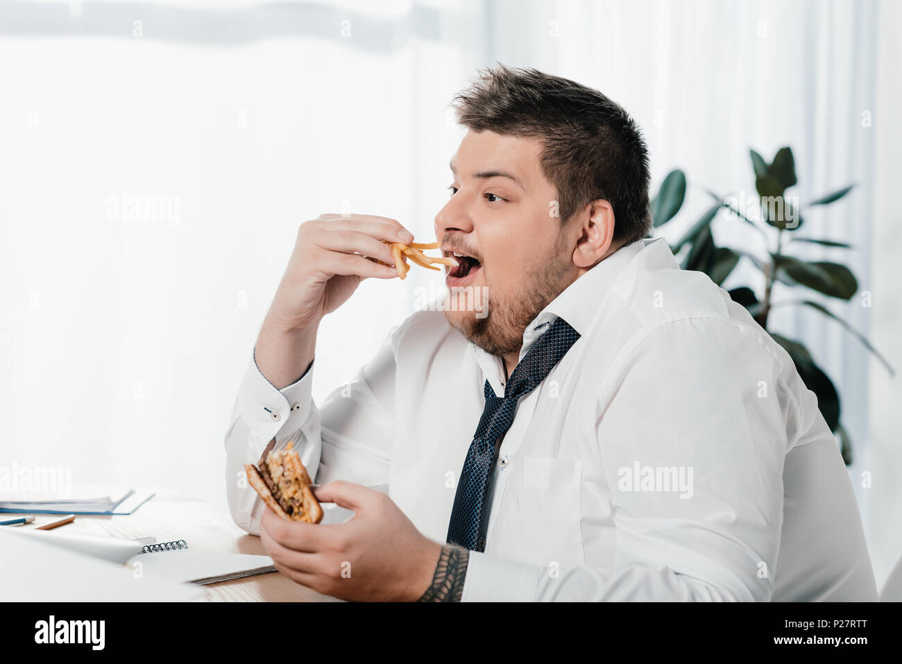 overweight businessman eating hamburger and french fries at workplace ...