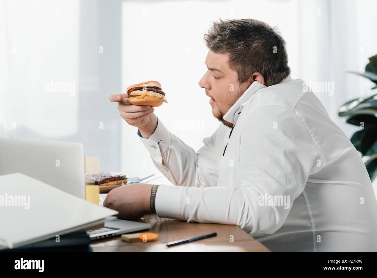 overweight businessman eating hamburger while working in office Stock ...