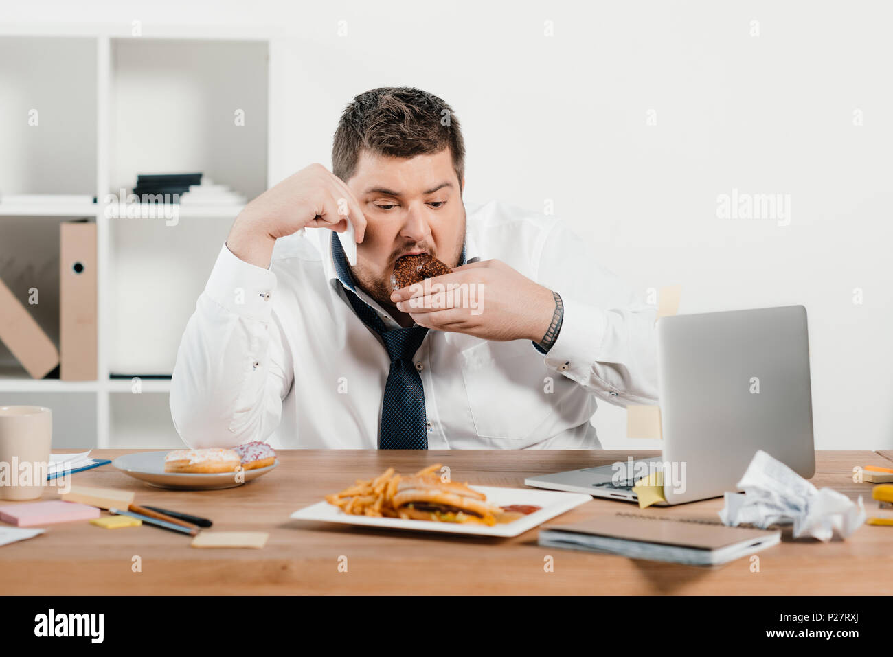 overweight businessman eating donuts, hamburger and french fries at ...