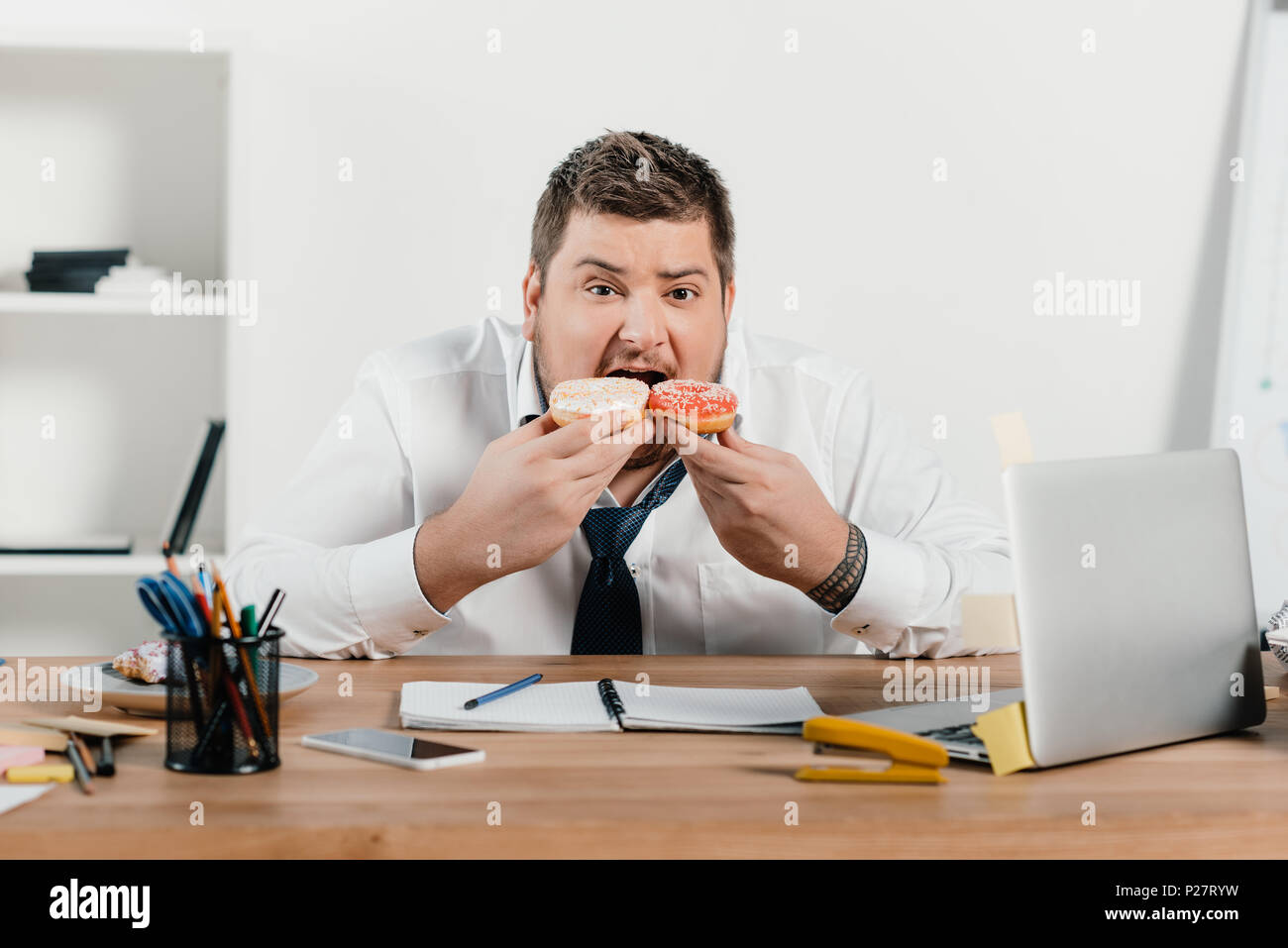 overweight businessman eating donuts at workplace with laptop Stock ...