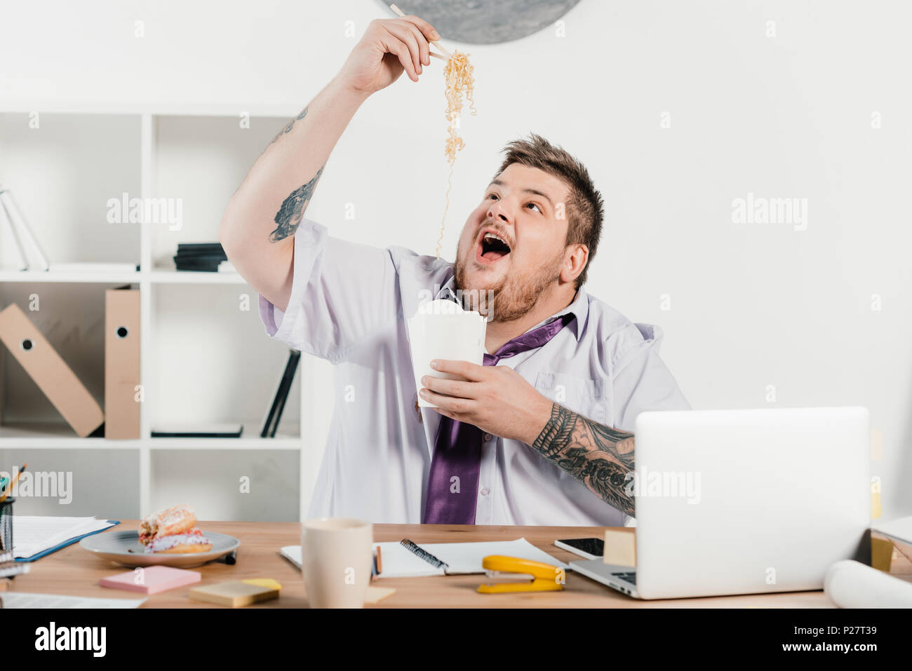 excited overweight businessman eating noodles at workplace in office ...