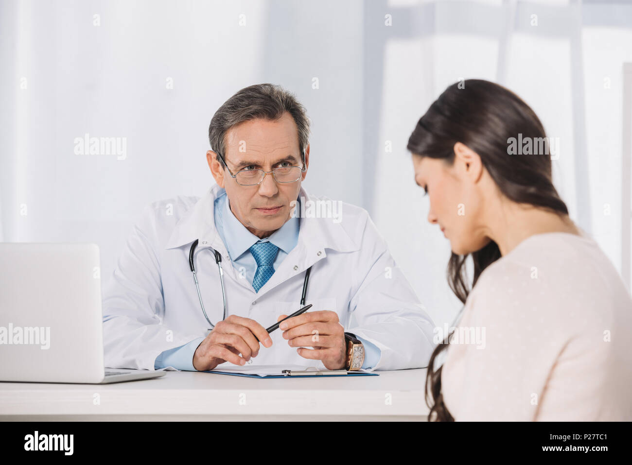 male serious doctor and female patient sitting at talking at clinic ...