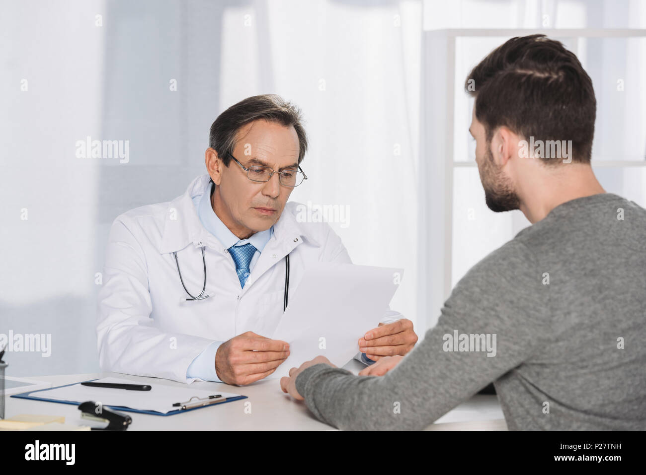 doctor reading male patient documents Stock Photo - Alamy