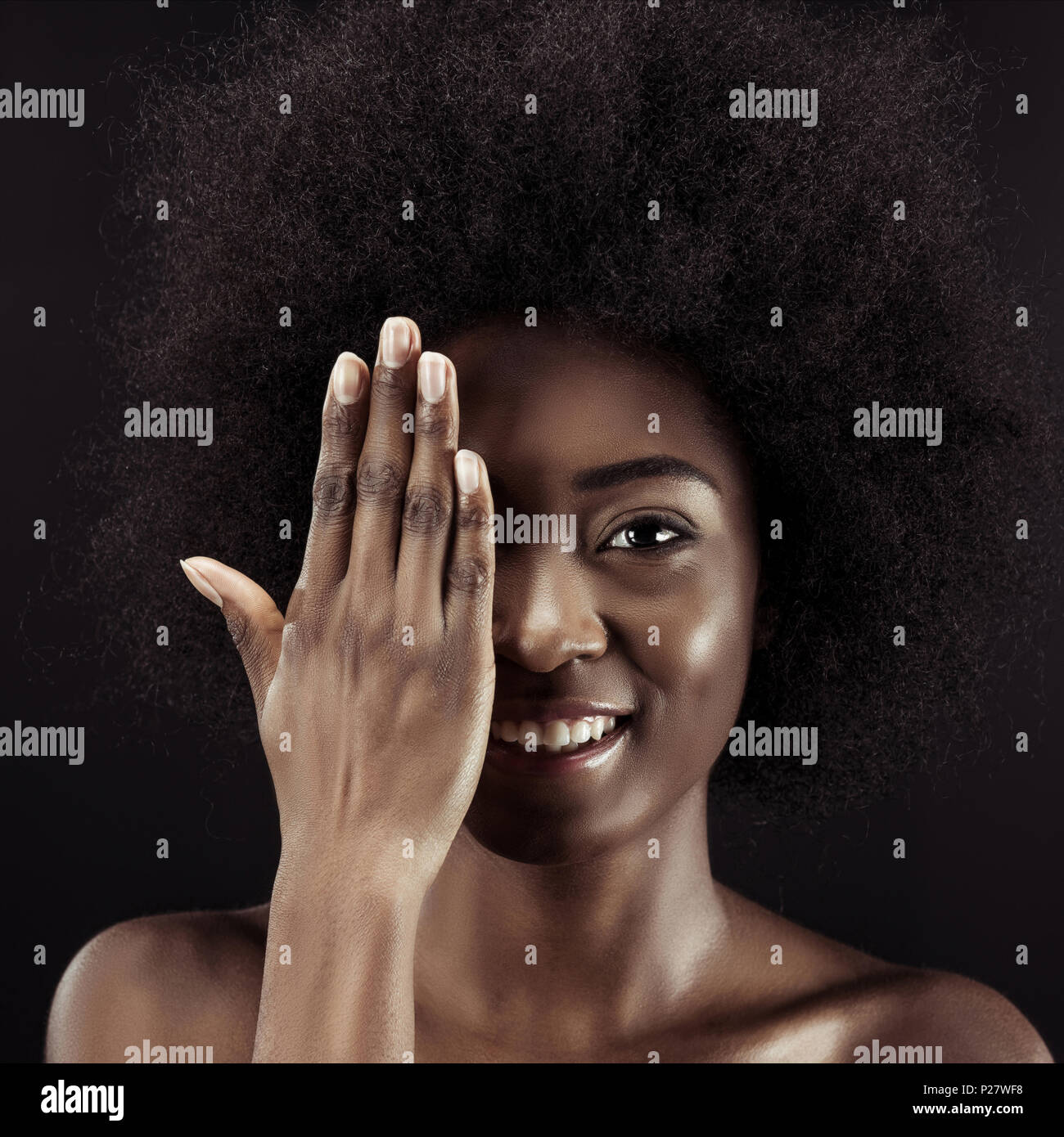 happy african american woman covering eye with hand isolated on black ...