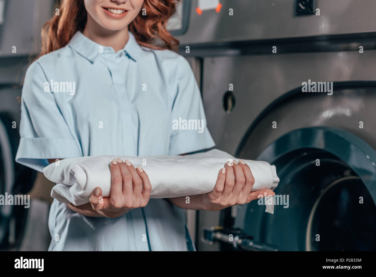 cropped shot of female dry cleaning worker holding stack of clean white ...