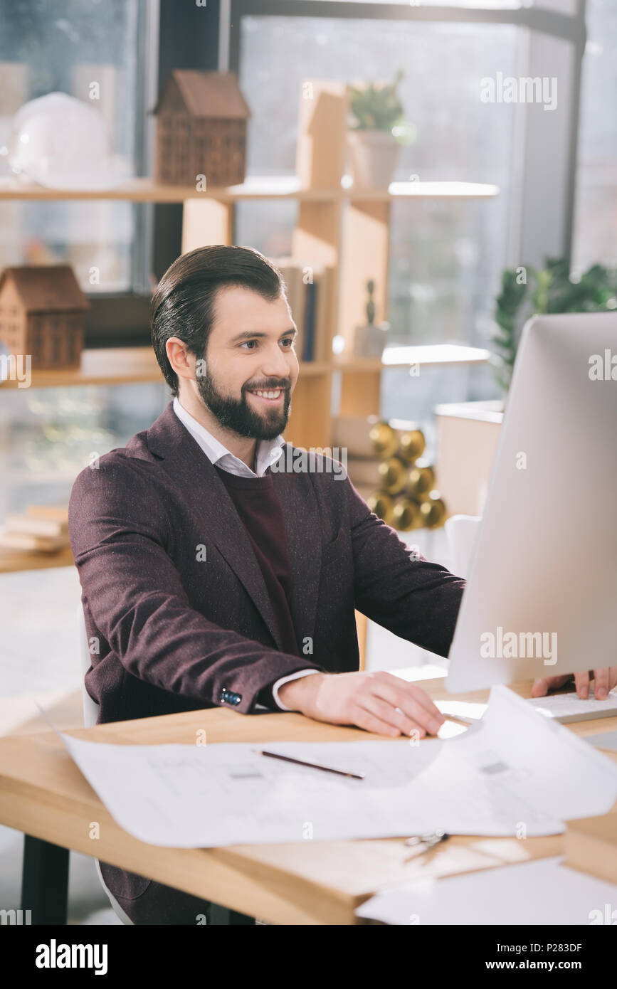 handsome architect sitting at workplace with computer and blueprints ...