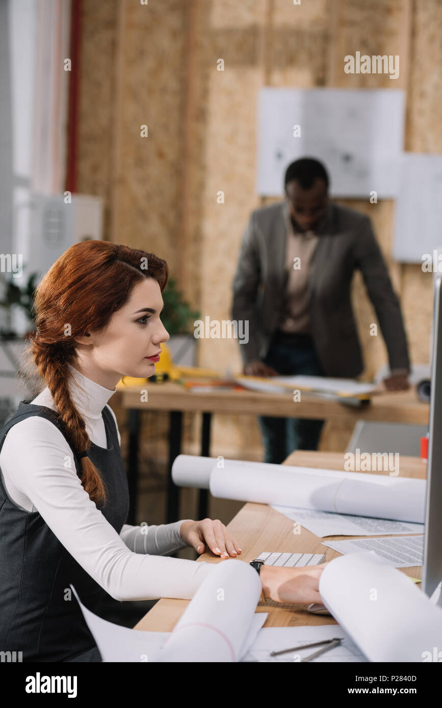 beautiful female architect using computer while her colleague standing ...