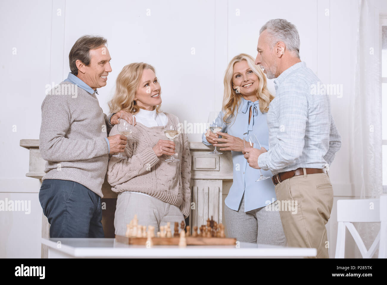 happy friends speaking and holding glasses in hands in room Stock Photo ...