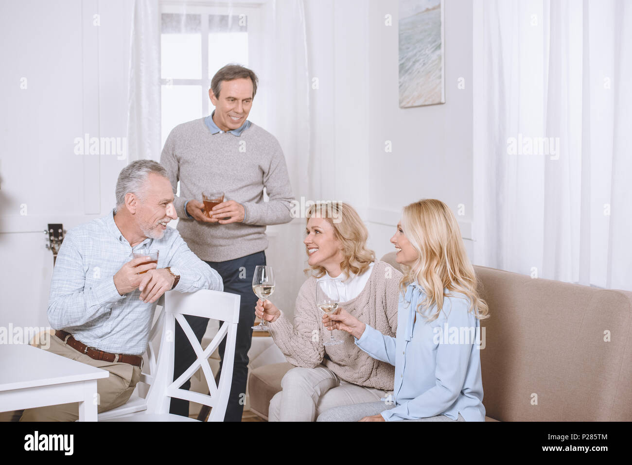 friends sitting on sofa and on chair while speaking in room Stock Photo ...