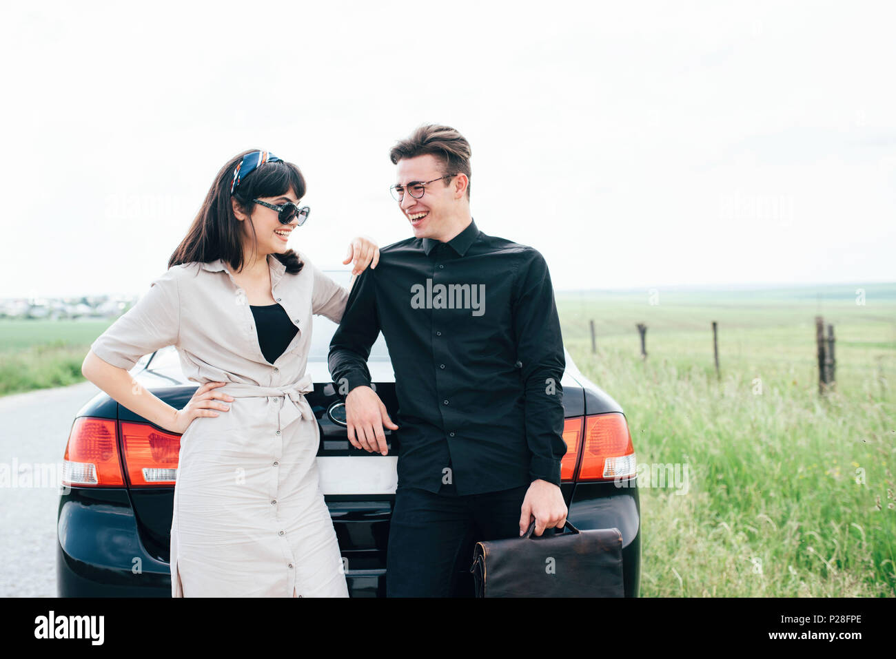 Couple young girl and boy talking around a black car on the background ...