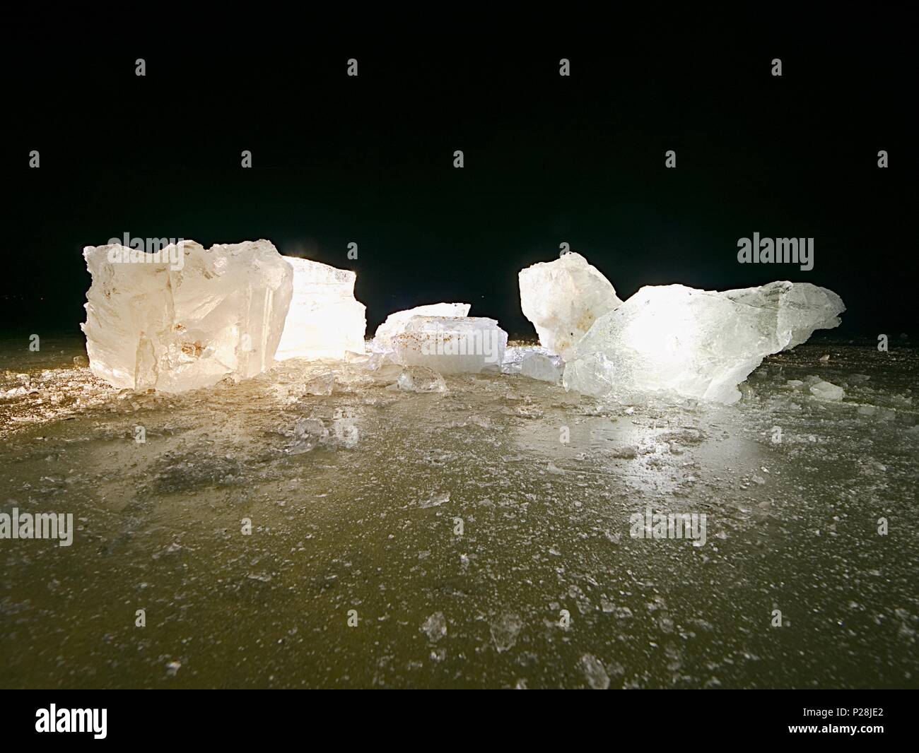 Blue ice cubes shine on flat glacier surface. Thanks to spot light ...