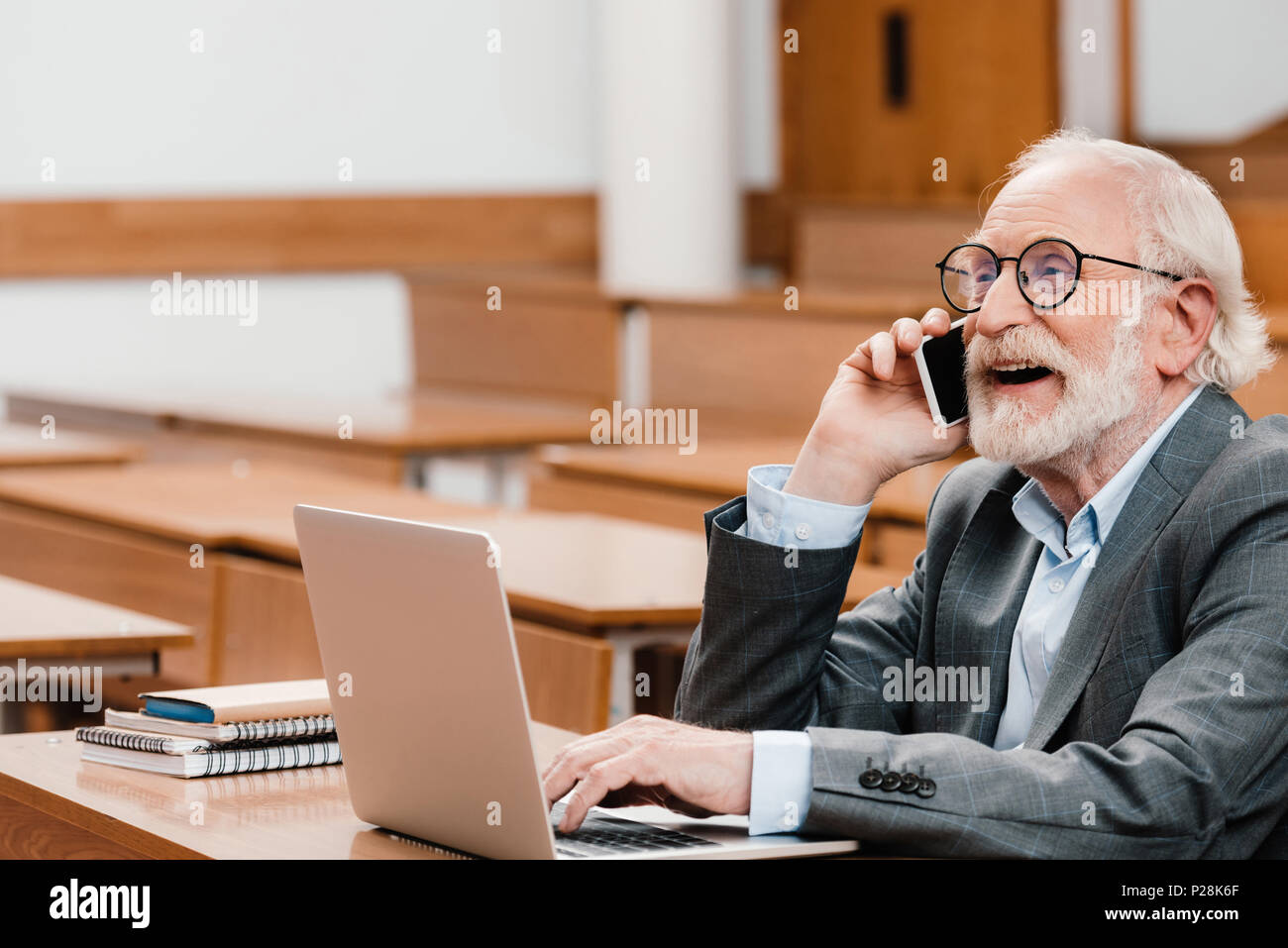 smiling grey hair professor sitting in empty lecture room and talking ...