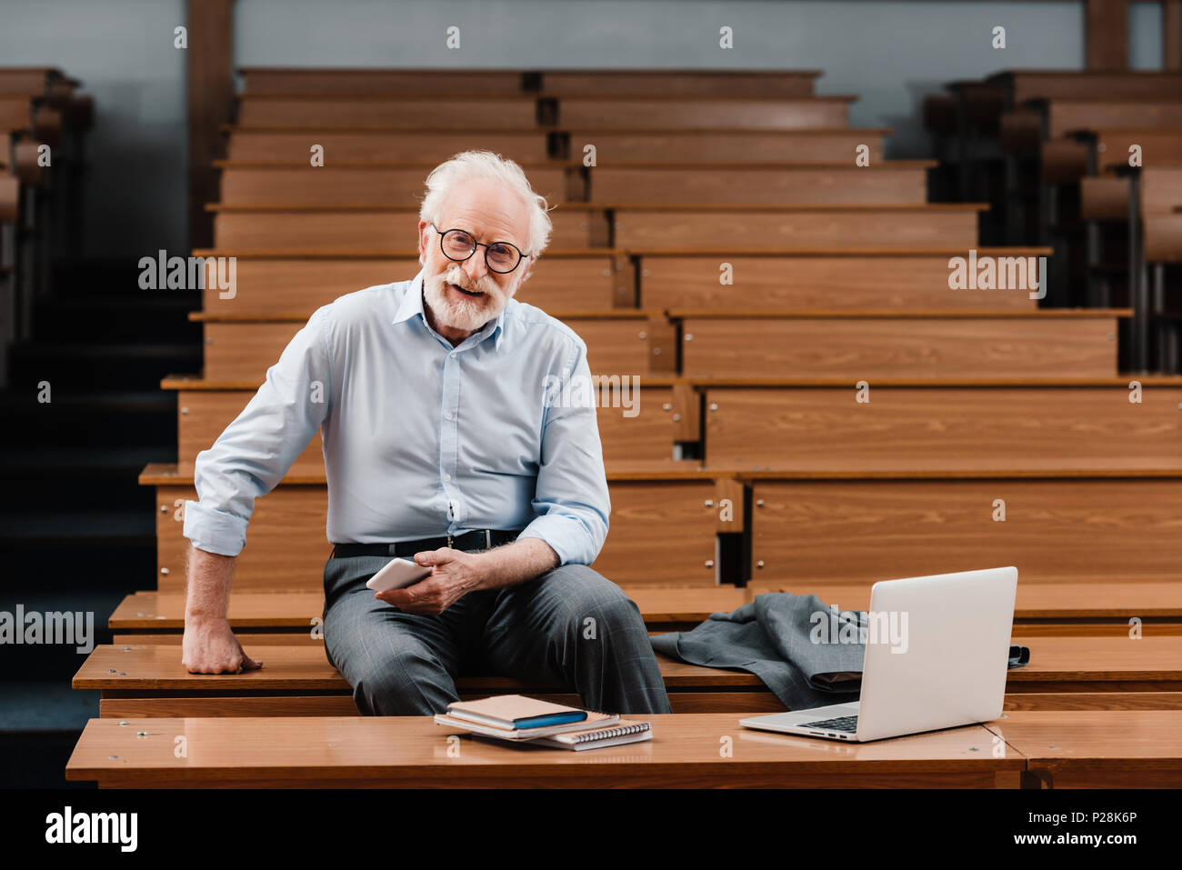 smiling grey hair professor sitting in empty lecture room Stock Photo ...