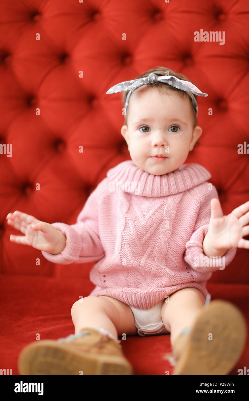 Little beautiful female baby sitting in red background on sofa Stock ...
