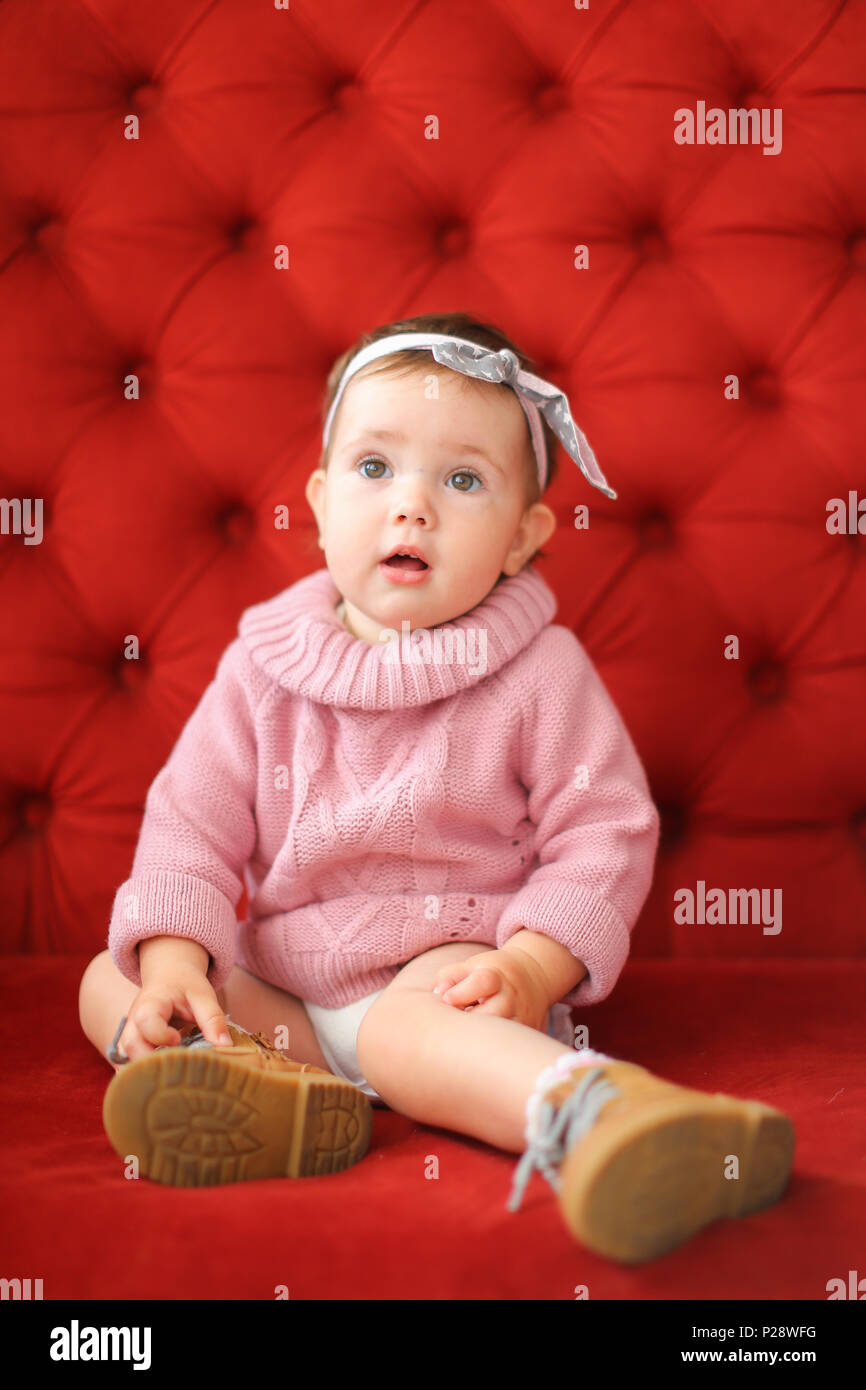 Little pretty female child sitting on sofa with red background Stock ...