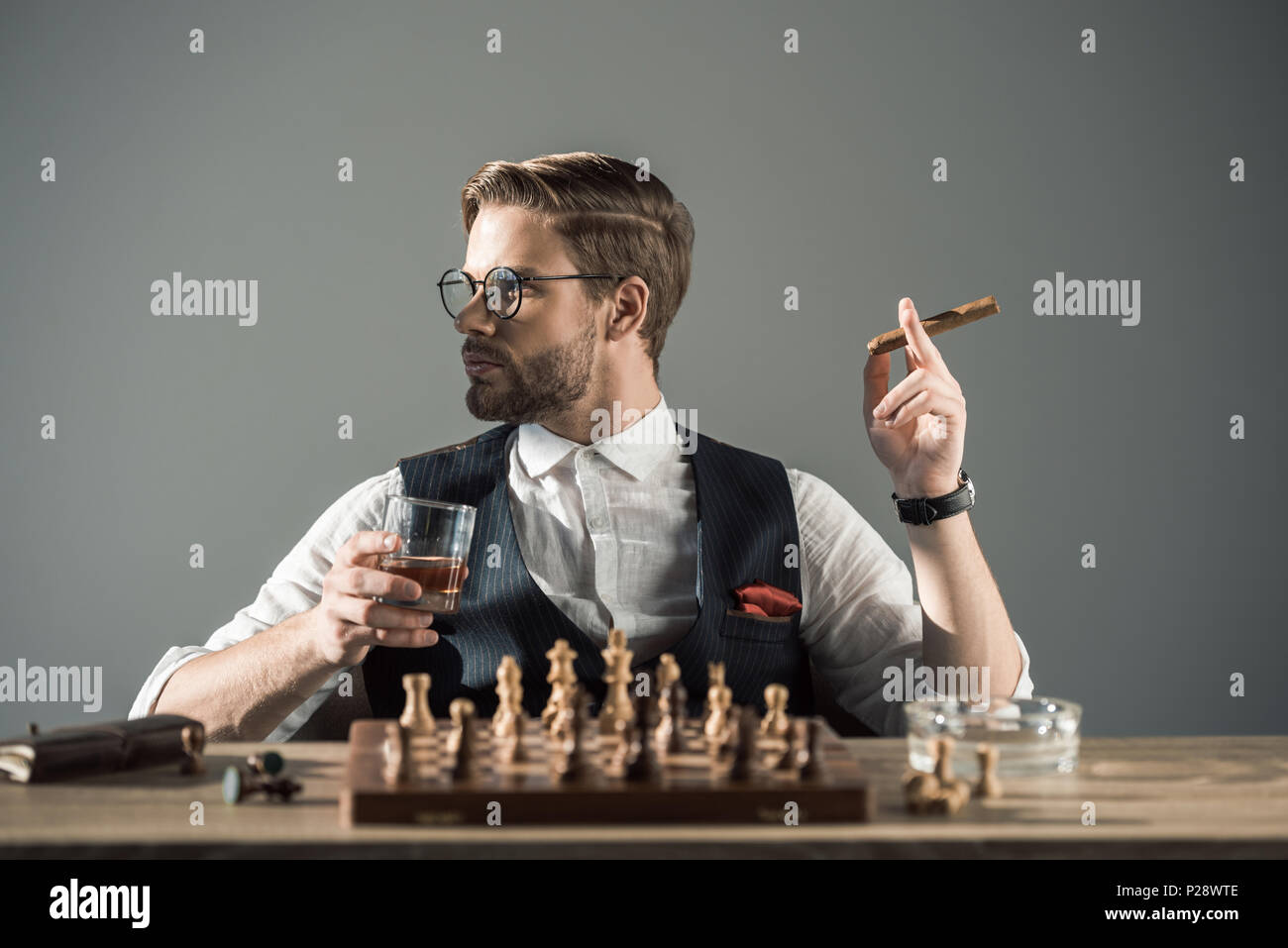 young man with glass of whisky smoking cigar and looking away while ...
