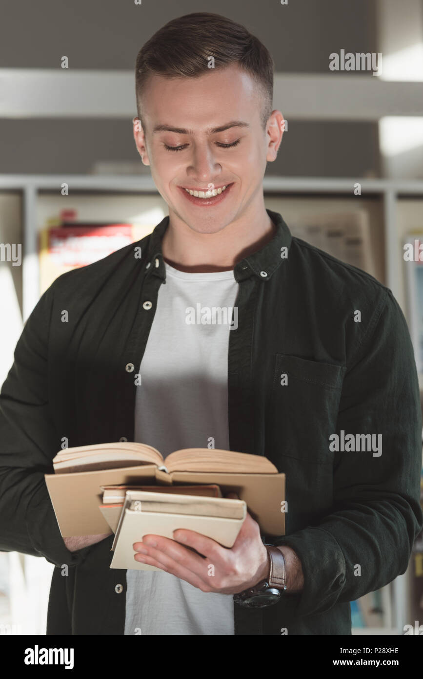 smiling handsome student standing and reading book in library Stock ...