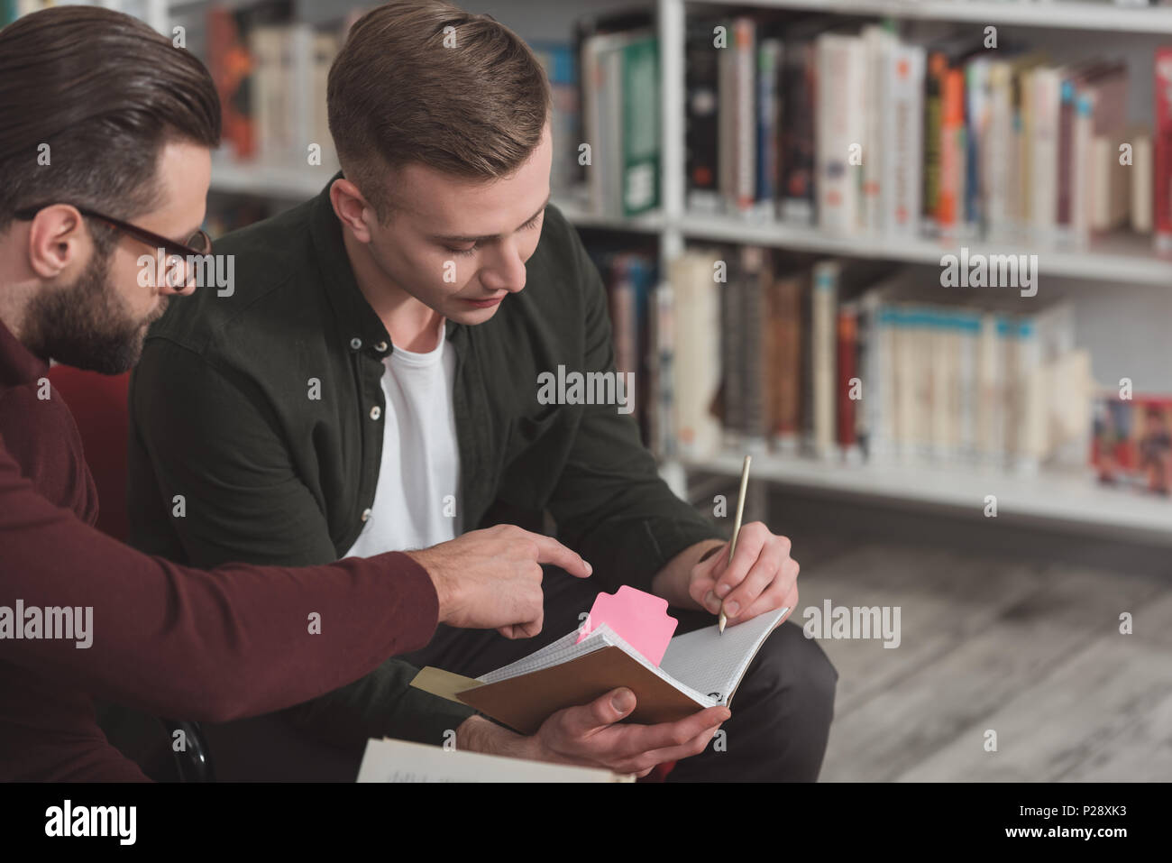 man pointing on something in friends notebook in library Stock Photo ...