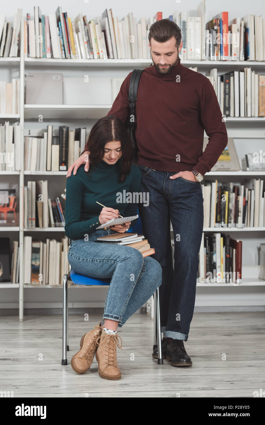 boyfriend standing near girlfriend writing something to notebook in ...