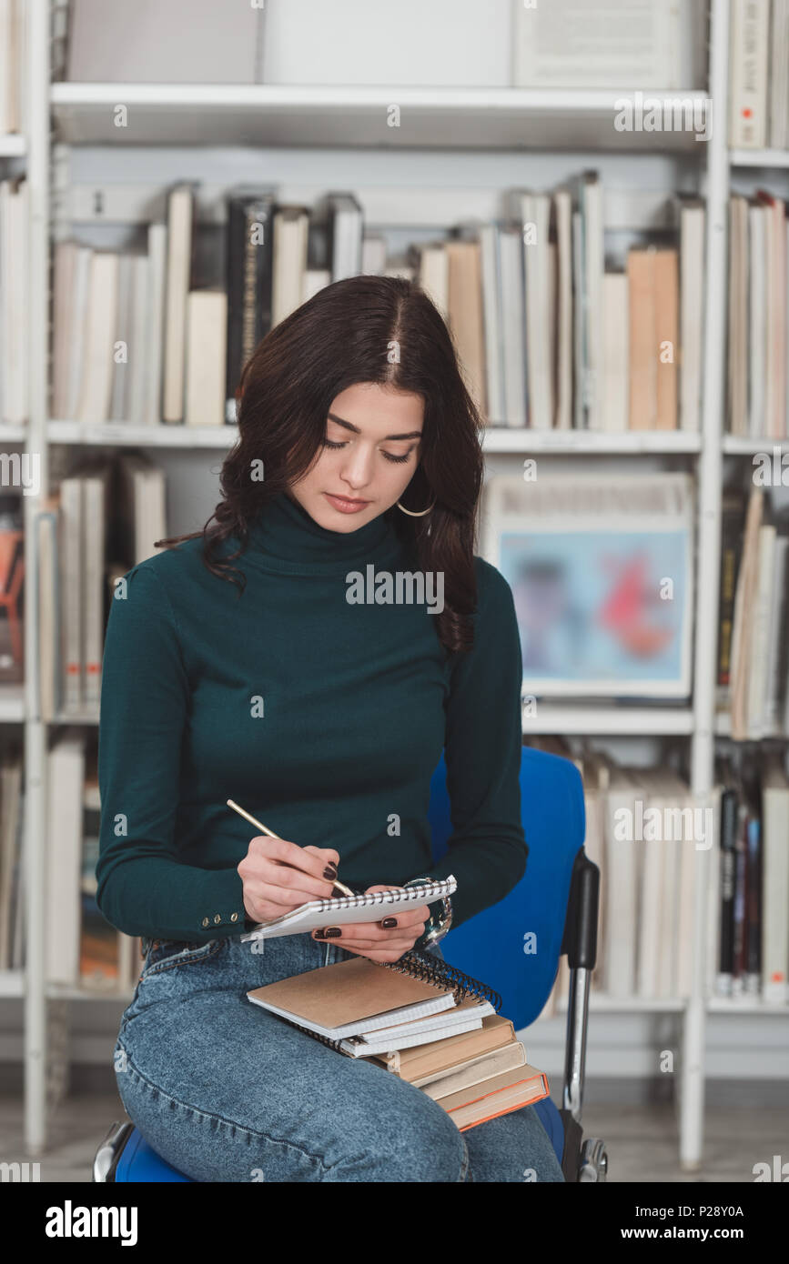 girl sitting on chair and writing something to notebook in library ...