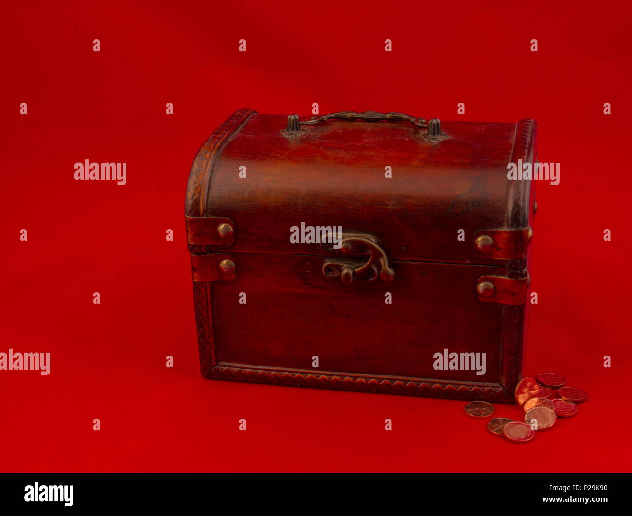 Small vintage wooden trunk with some gold coins isolated on a red ...