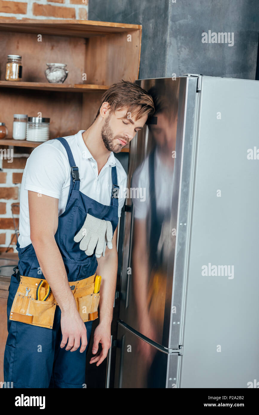tired young foreman with tool belt leaning at broken refrigerator Stock ...