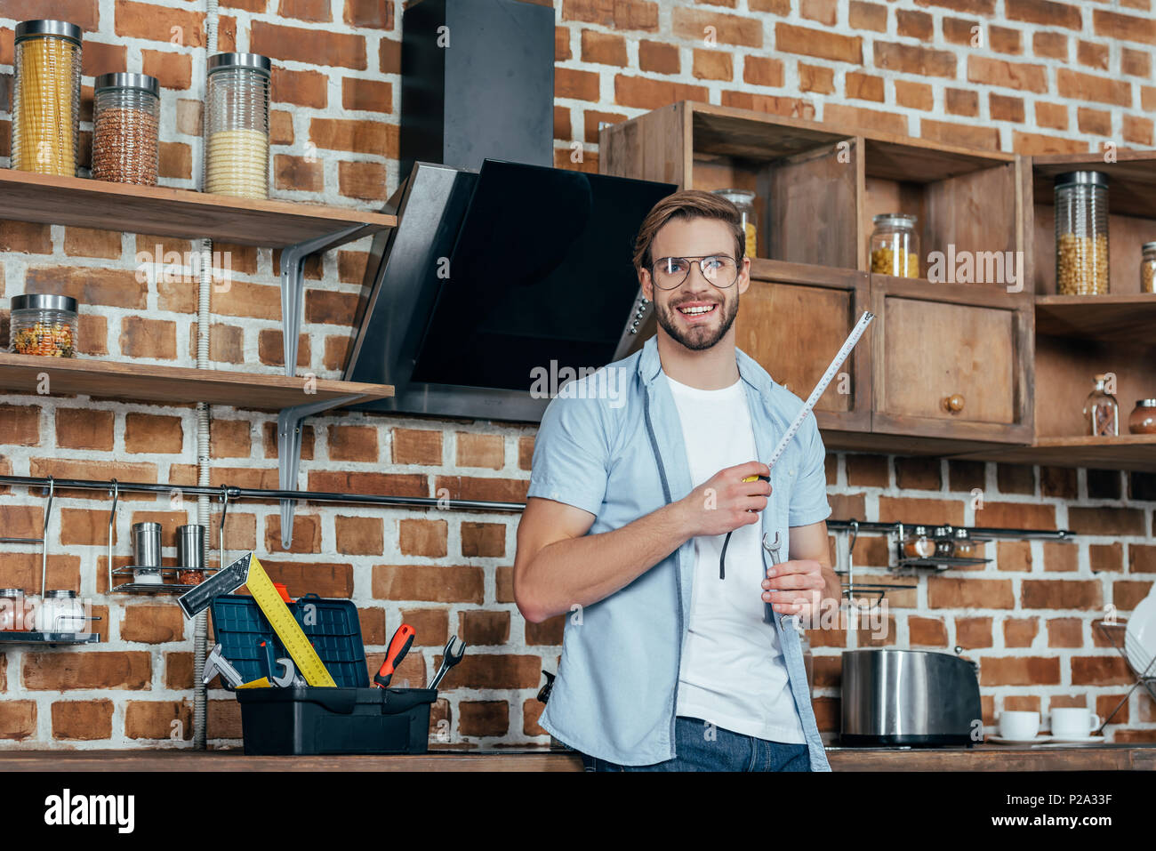young man holding measuring tape and smiling at camera while repairing ...