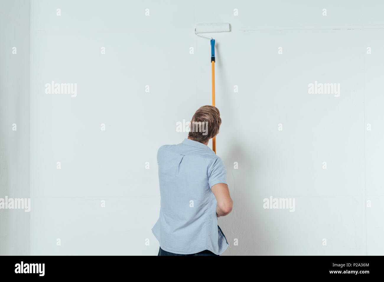 back view of young man using paint roller while painting wall at home ...