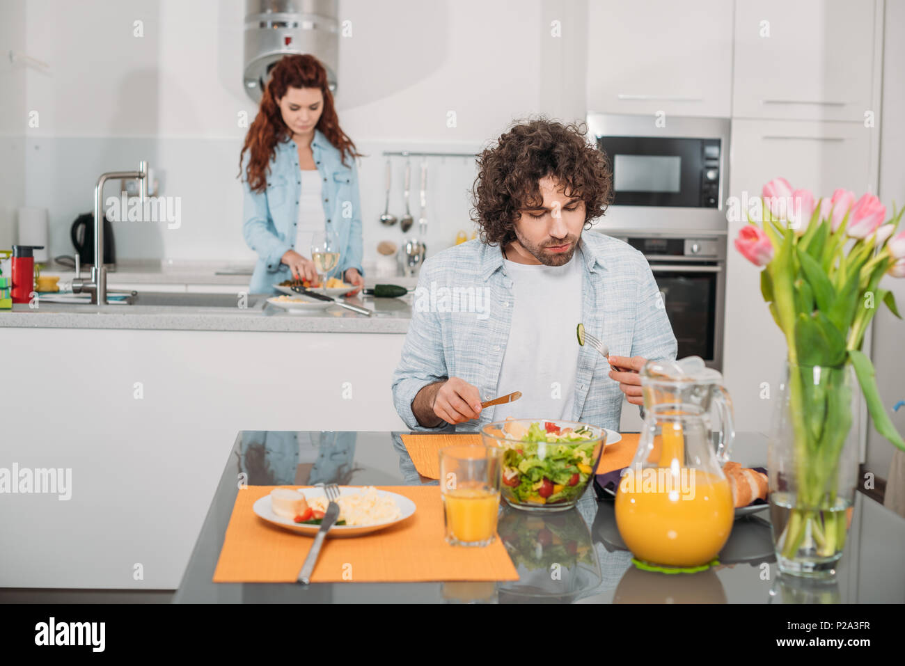 boyfriend eating while girlfriend cooking at kitchen Stock Photo - Alamy