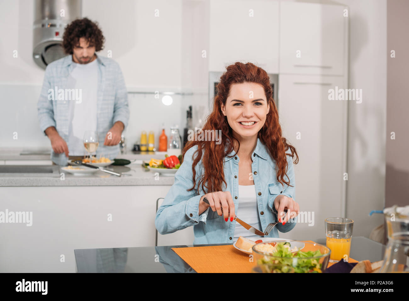smiling girlfriend eating while boyfriend cooking at kitchen Stock ...