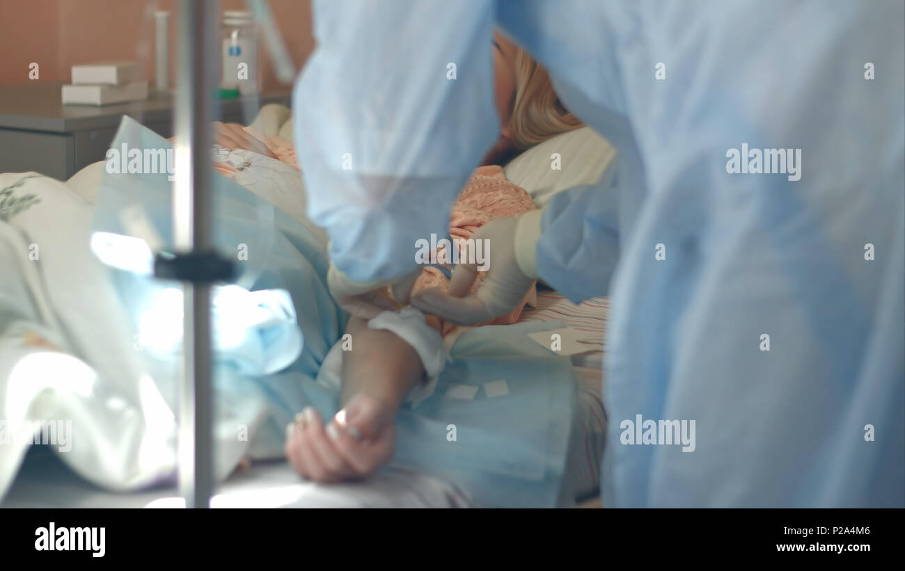 Nurse in gloves and mask putting female patient on a drip in a hospital ...