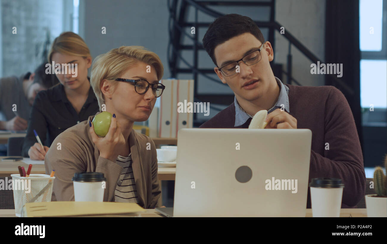 Young business partners are resting in office, eating fruits and ...