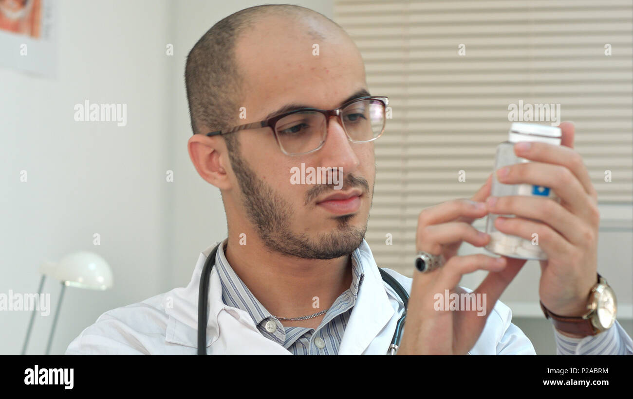 Male doctor attentively reading medicine label of a bottle of pills ...