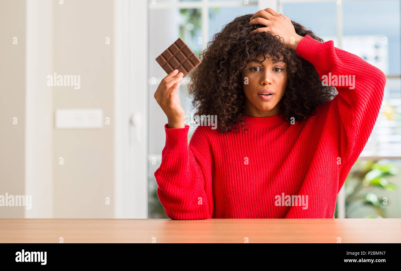 African american woman eating chocolate bar at home stressed with hand ...