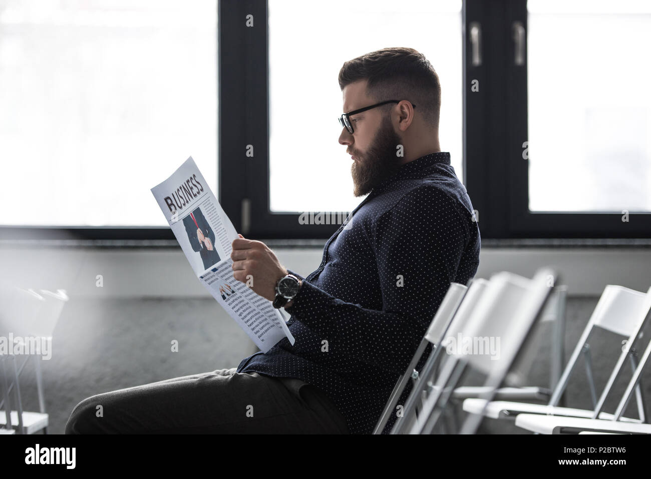 side view of focused businessman reading newspaper while sitting in ...