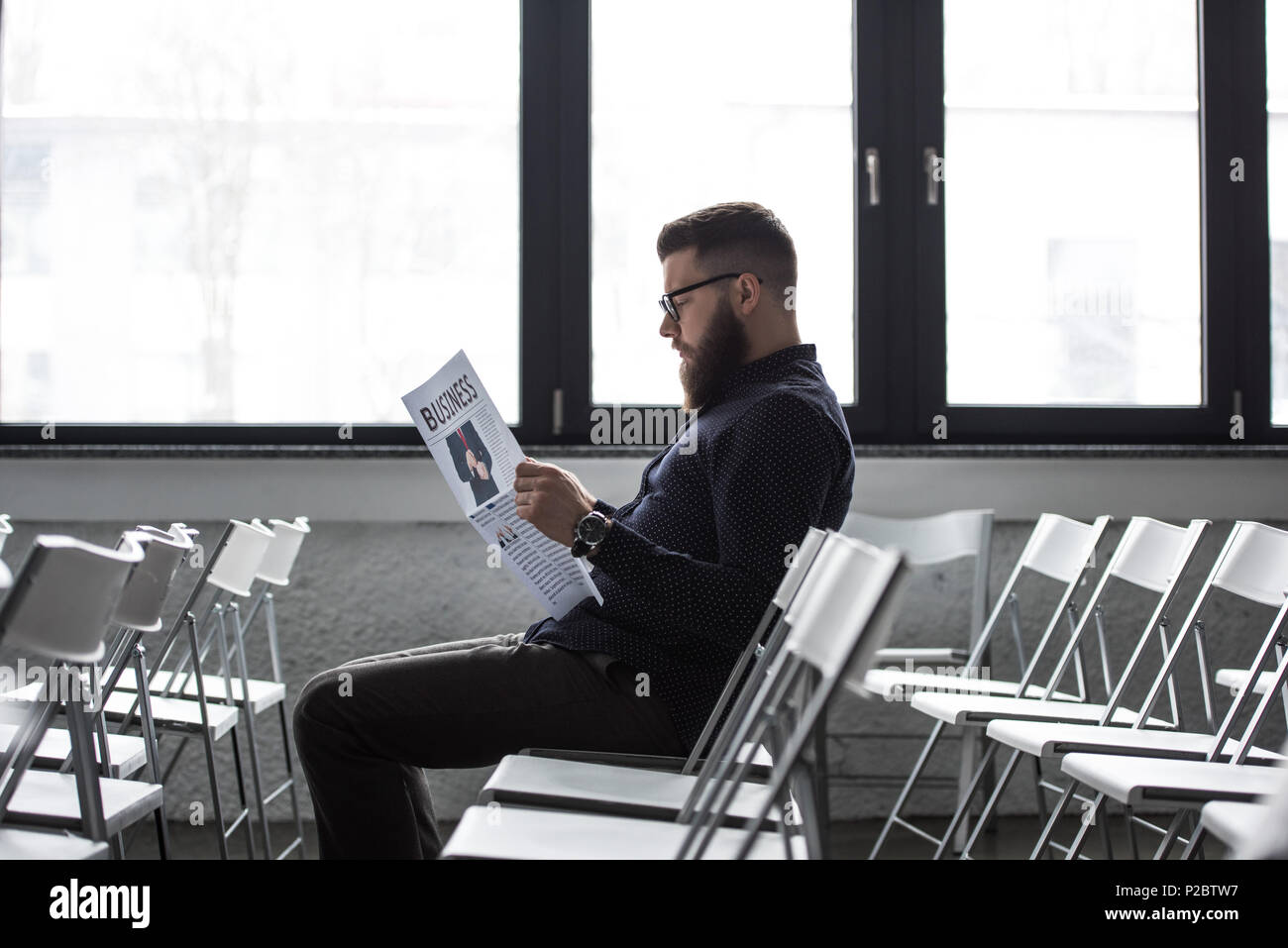 side view of focused businessman reading newspaper while sitting in ...