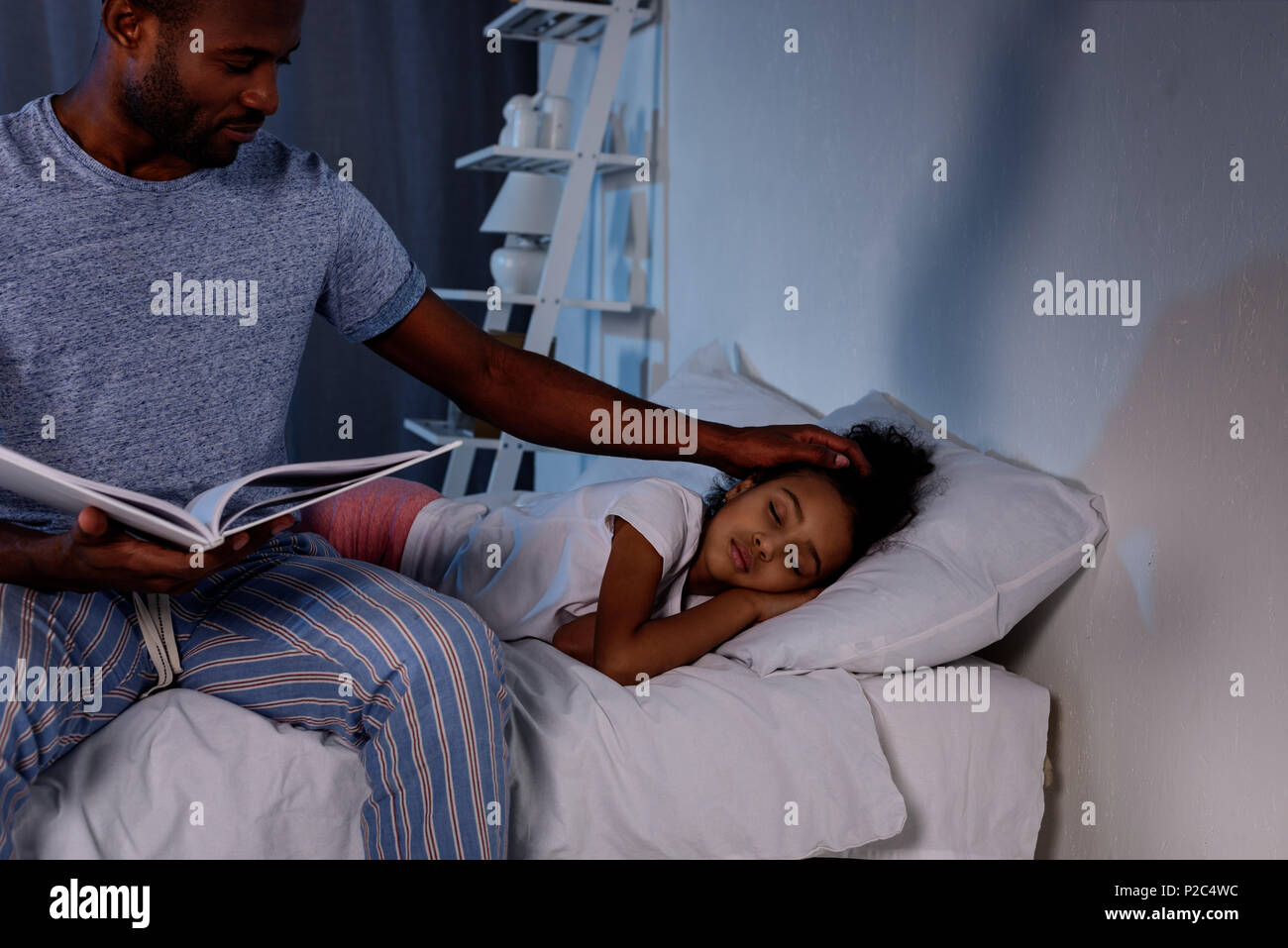 African American Father Holding Book And Palming Sleeping Daughter At