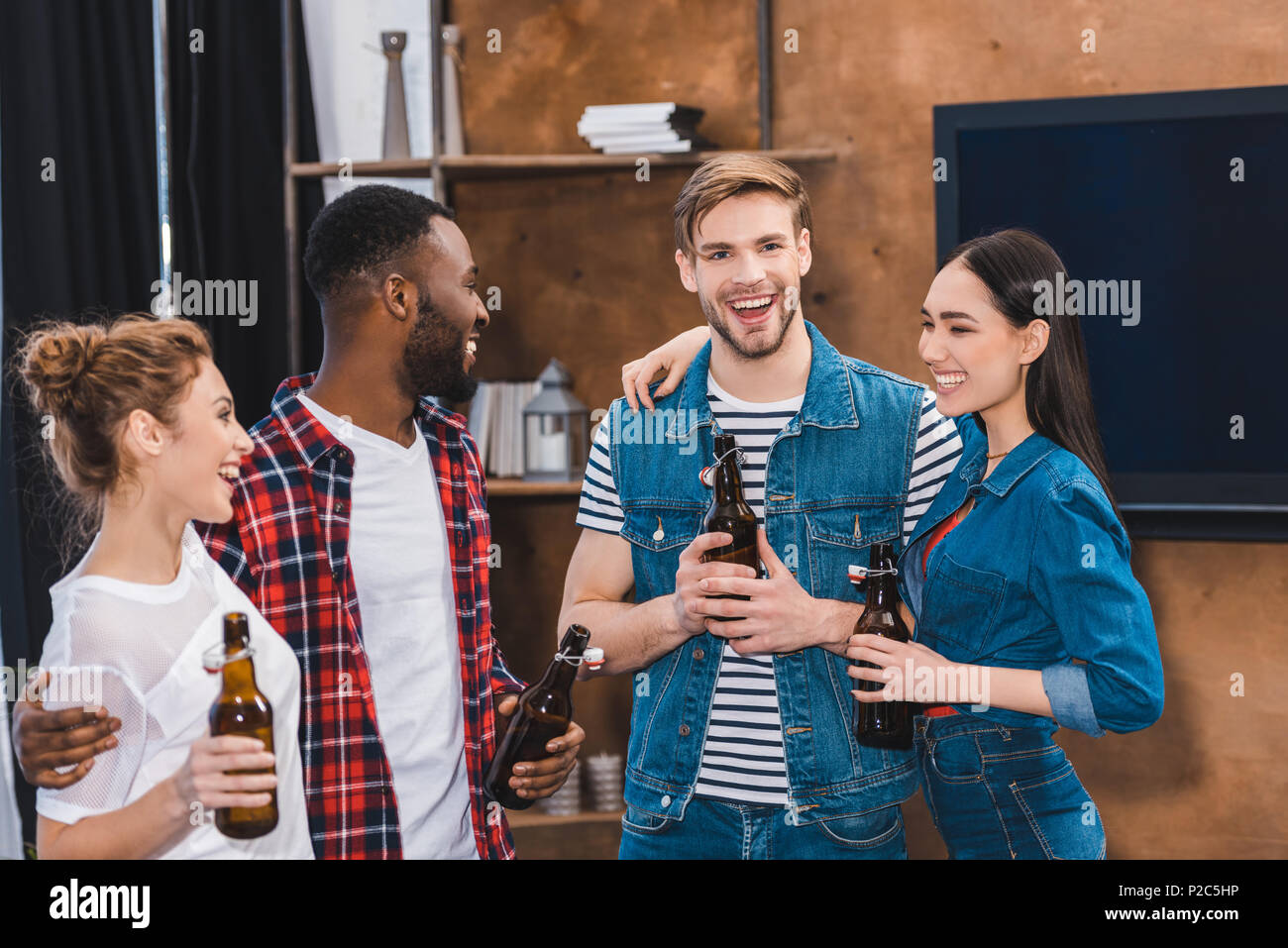 happy young multiethnic friends holding beer bottles and talking ...