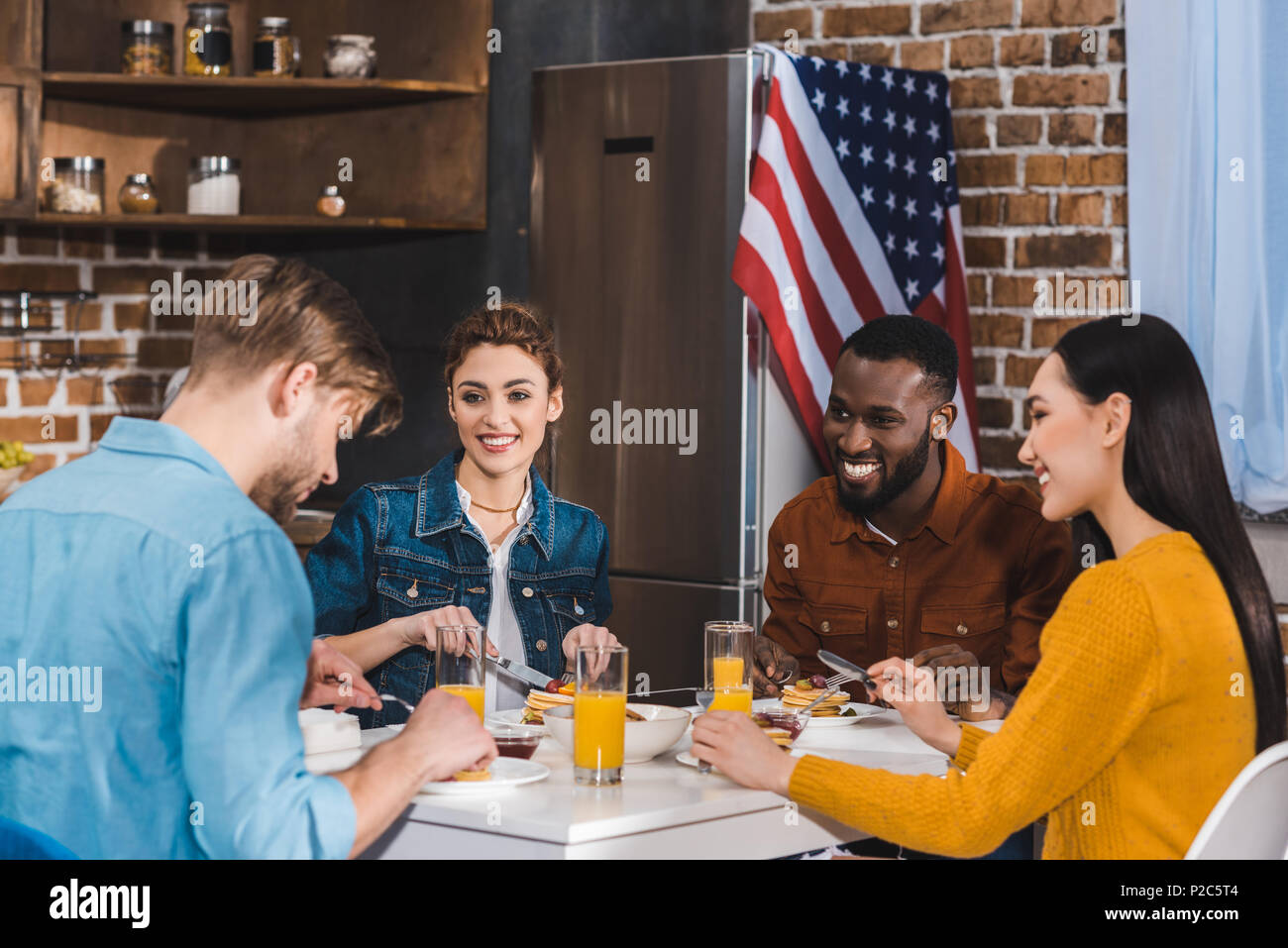happy young multiethnic friends eating pancakes and drinking juice ...