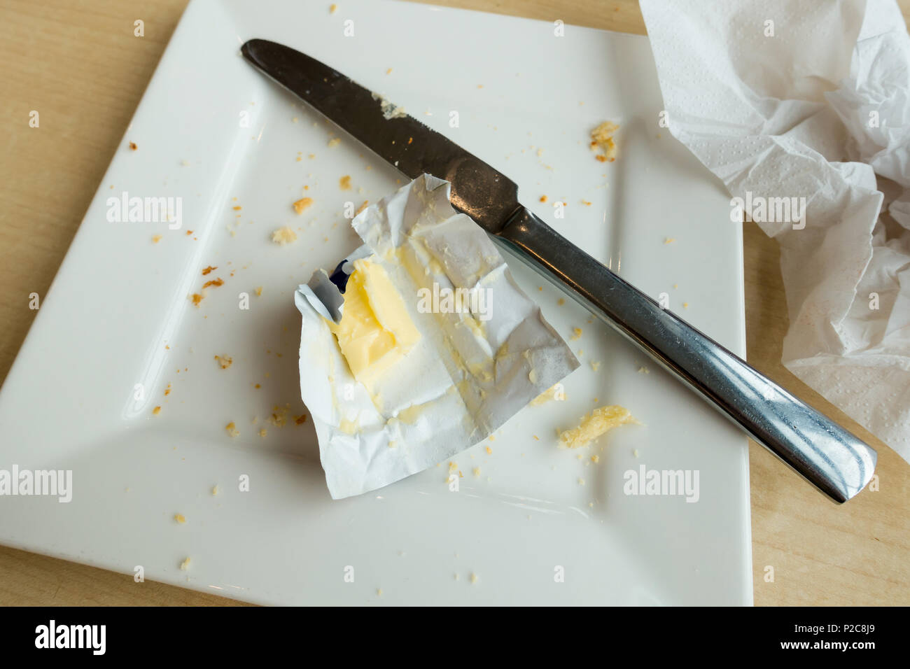 An empty plate with crumbs, a knife & leftover butter with a crumpled ...
